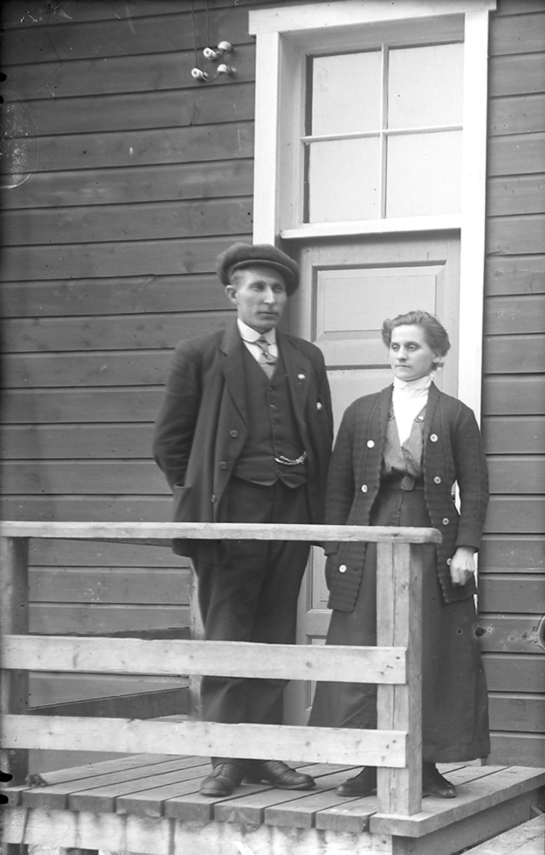 Portrett. Par i 30-40-åra. Står ute på en trapp. Dør bak dem.Bildet er ...