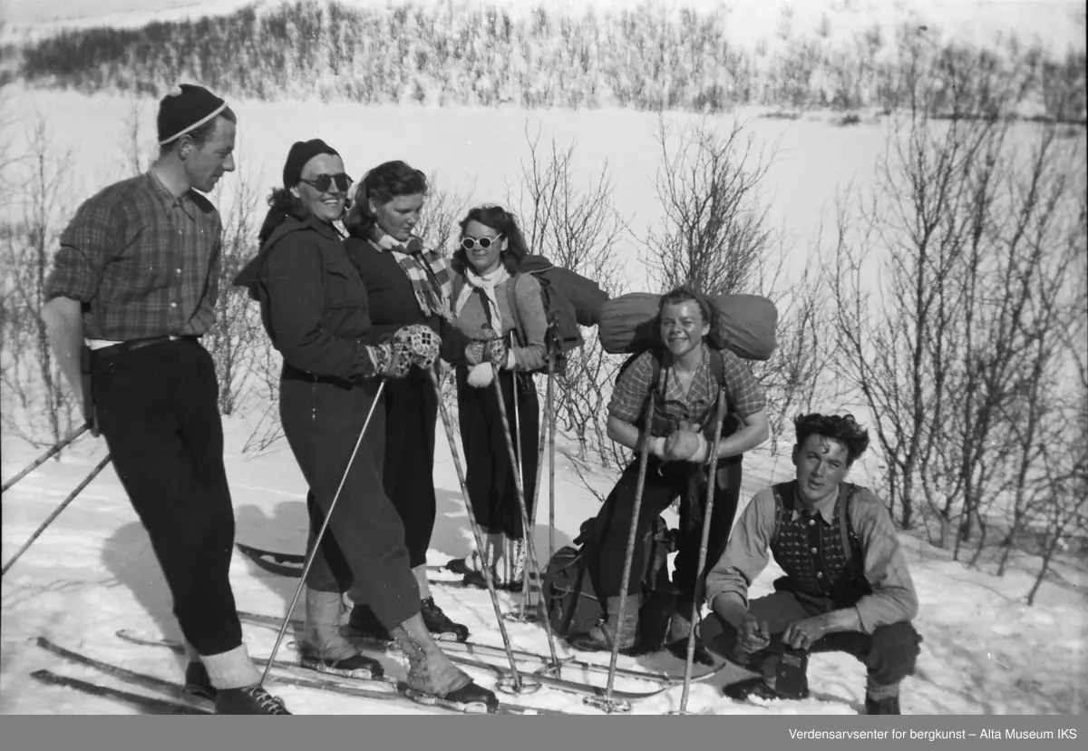 Seks personer i påskesolen står ved et fjellvann og tar en pust i bakken. - Verdensarvsenter for ...