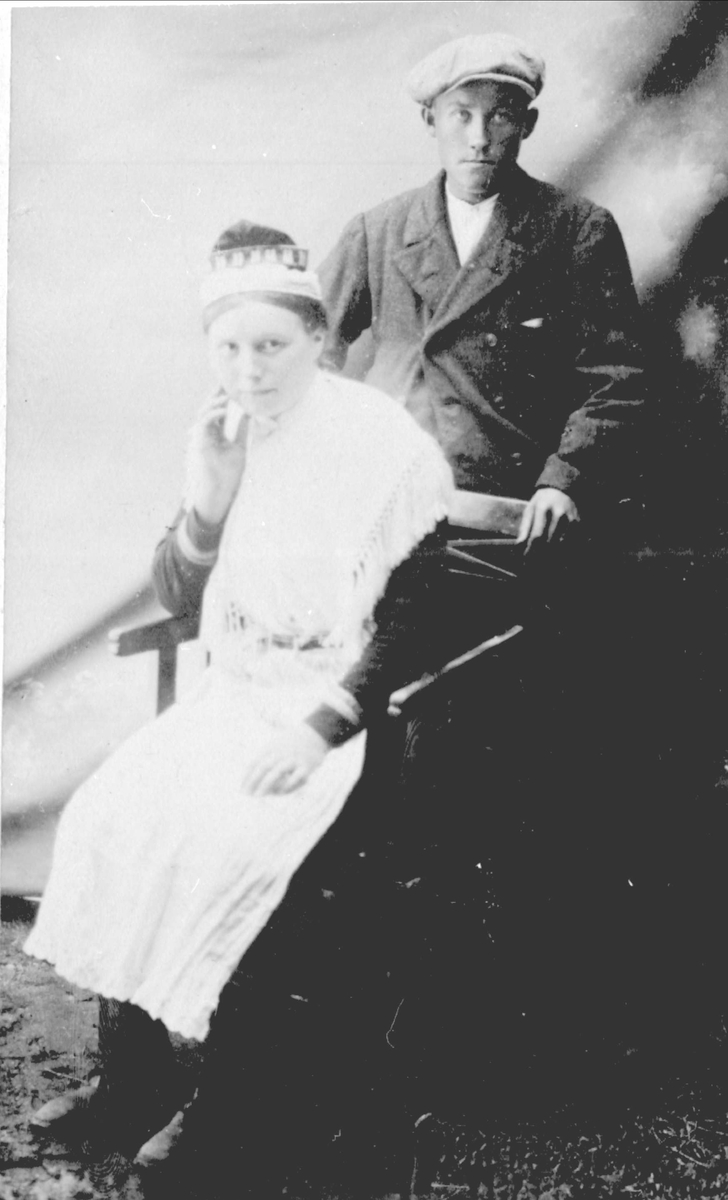 Studioportrett i helfigur av kvinne sittende i stol og mann stående bak ...