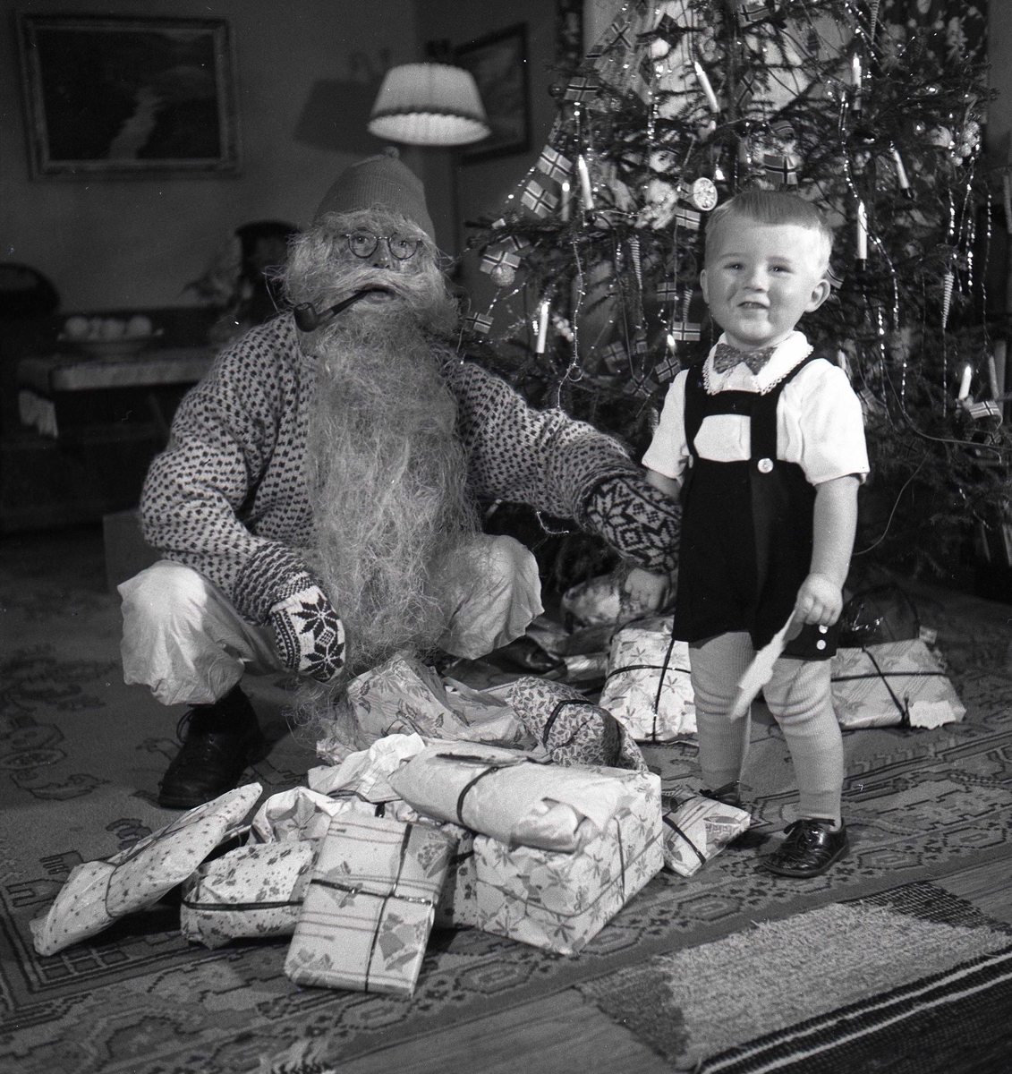 Gutt stående med mann utkledd som julenisse ved siden av seg. I ...