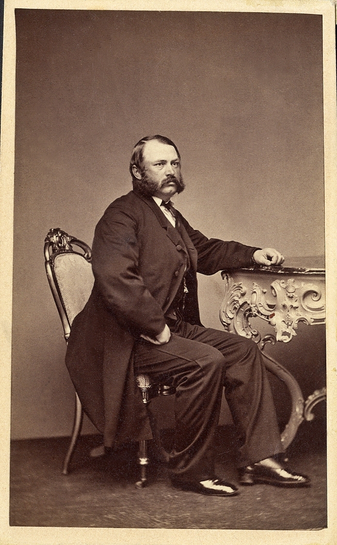 Porträttfoto av en man i mörk redingot med väst, stärkkrage och fluga ...